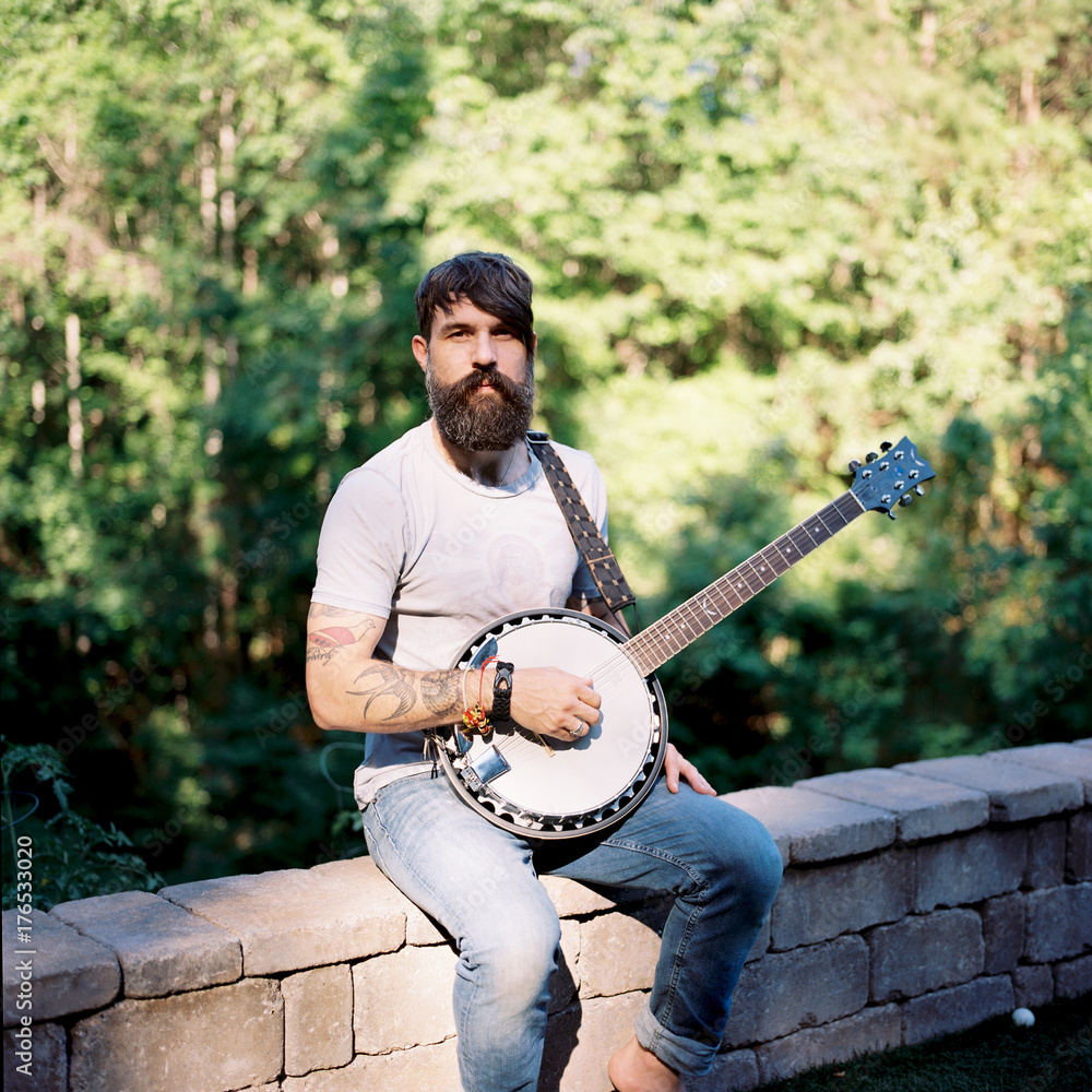 Bearded man sitting on a ledge playing a banjo Stock Photo | Adobe Stock