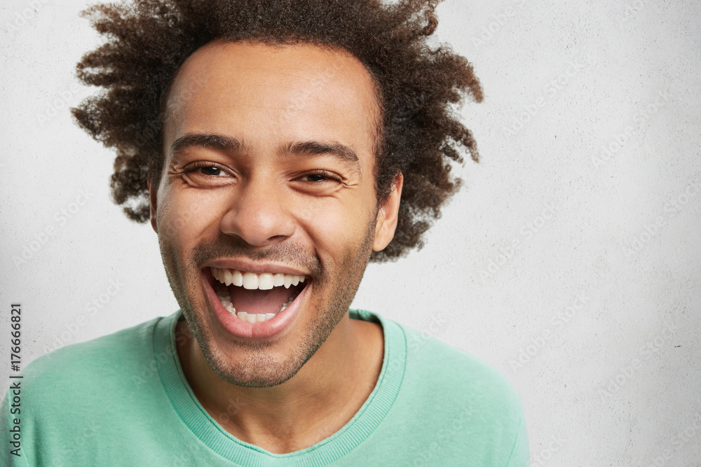 Overjoyed happy man with dark skin and bushy hairstyle, grins at camera ...