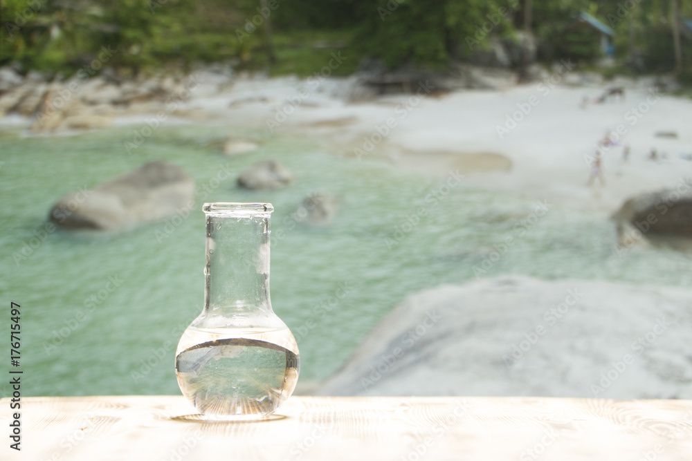 Clean water in a glass laboratory flask on wooden table on sea ...