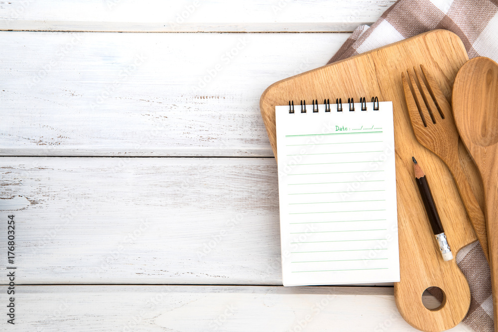 Notepad on chopping board with the wooden fork and spoon on white table ...