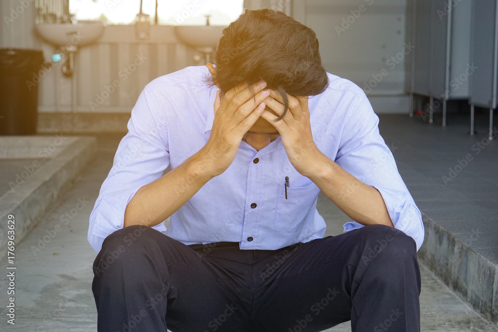 Depressed man holding the forehead with two hands sitting on the ladder ...