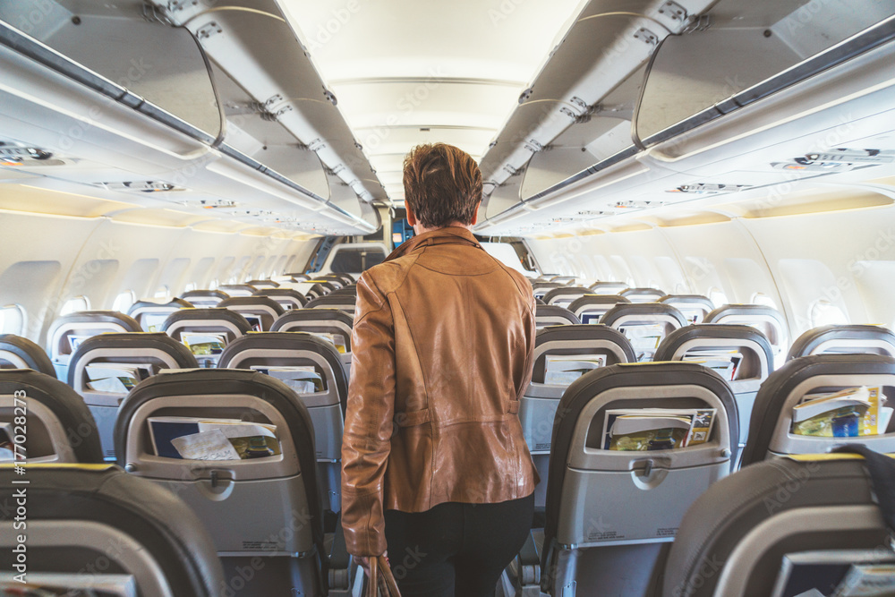 Woman walking down the aisle of an airplane Stock Photo | Adobe Stock