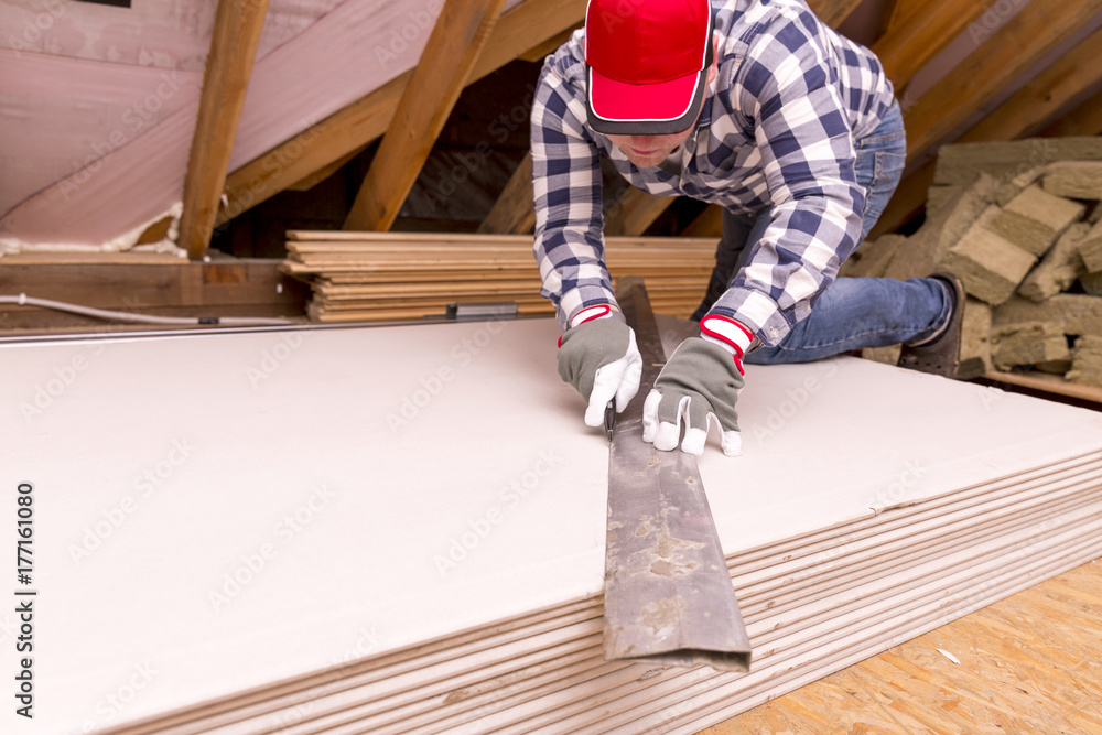 worker cutting plasterboard with construction knife. Attic renovation ...