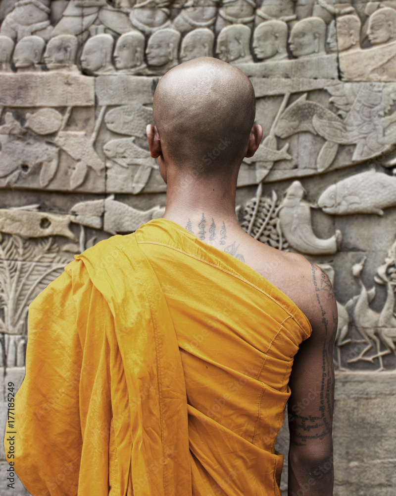 Buddhist monk standing in front of wall carvings. Bayon Temple. Angkor ...