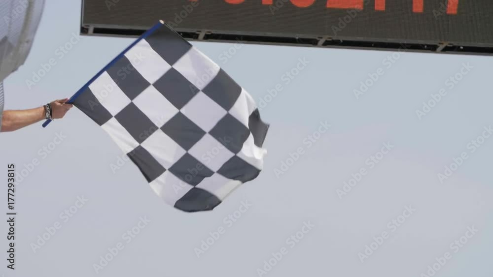 Man holding and waving Checkered race flag in slow motion at finish line on a raceway. Victory ...