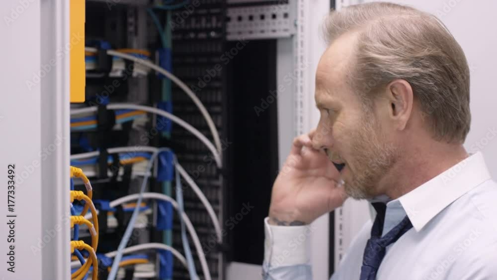 Computer engineer working on laptop and talking on phone, checking the ...