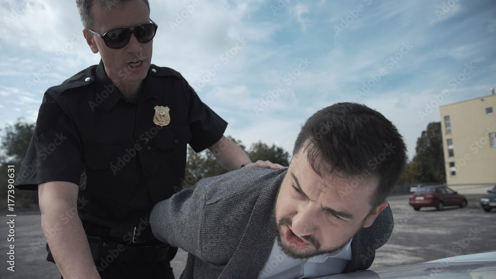 Police officer arresting criminal, putting him on car trunk and reading ...