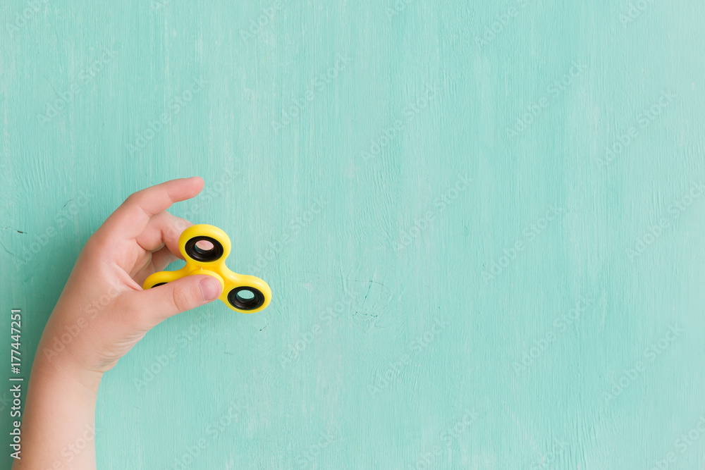 Child's hand spinning a fidget spinner device on turquoise background ...