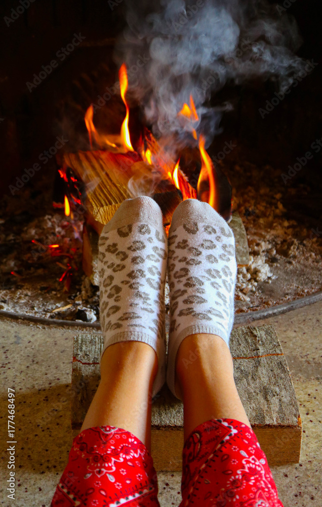 Burning wood at the fireplace, female legs in socks warming up ...