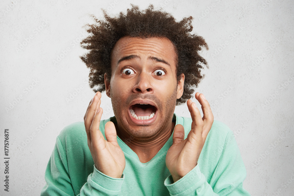 Portrait of dark skinned mixed race Afro American male looks with surprsied expression, has ...