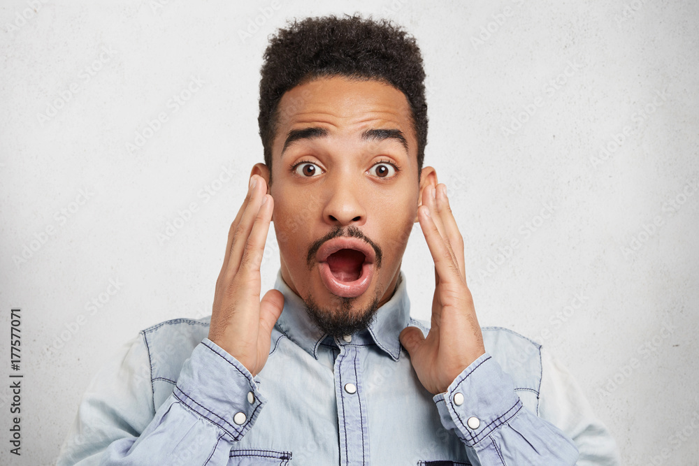 Omg, what I see! African astonished man has shocked expreesion, looks with wide open eyes and ...