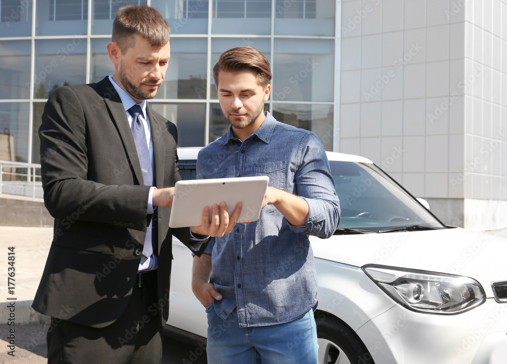 Salesman with tablet and client standing near new car outdoors Stock ...
