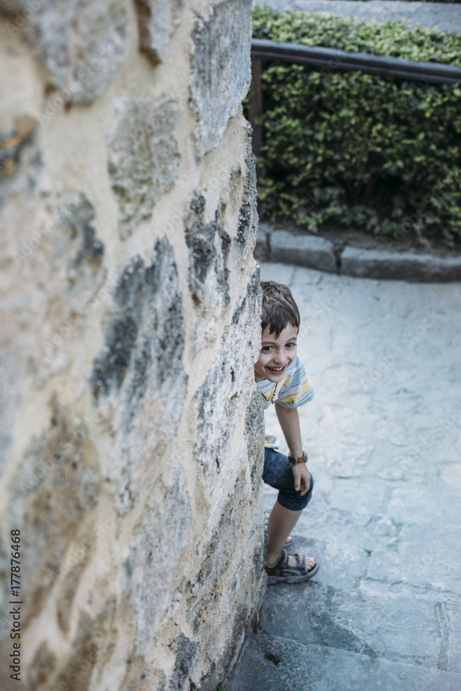 Boy playing hide and seek, laughing behind a wall, only face and a leg ...