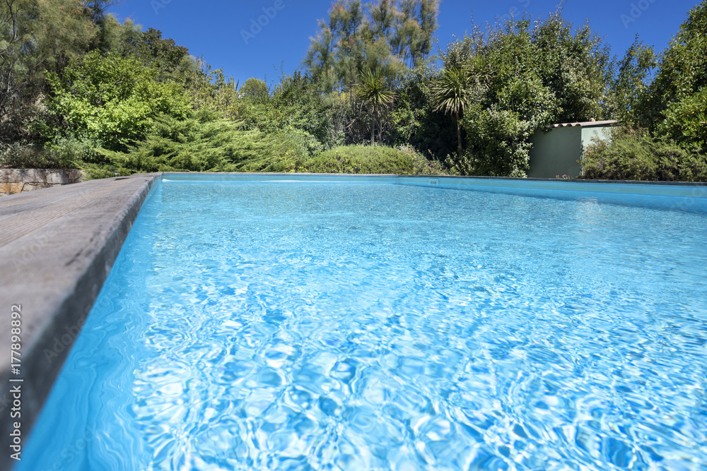 Surface of an empty swimming pool in a garden with clear cyan blue ...