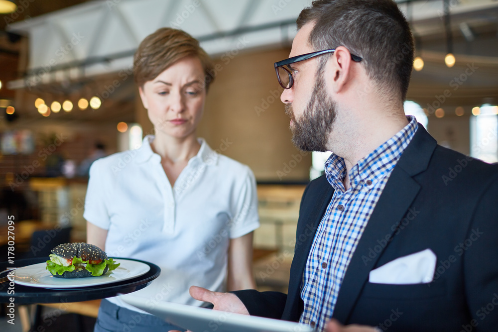 Bearded young restaurant manager talking to pretty waitress holding ...