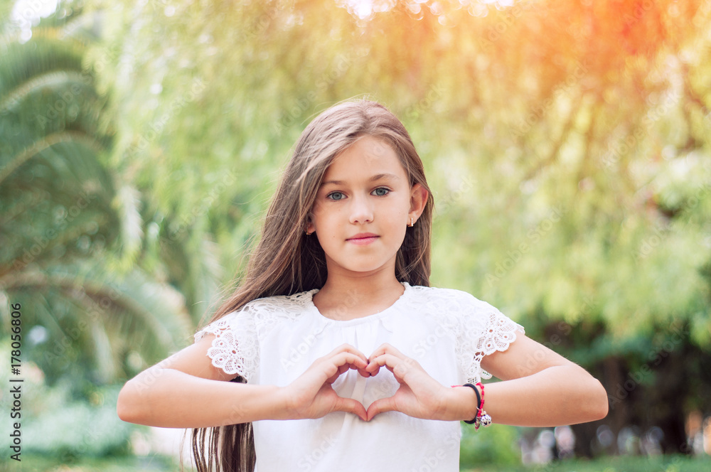 Hand love. Pretty little girl showing a heart symbol in the park on ...
