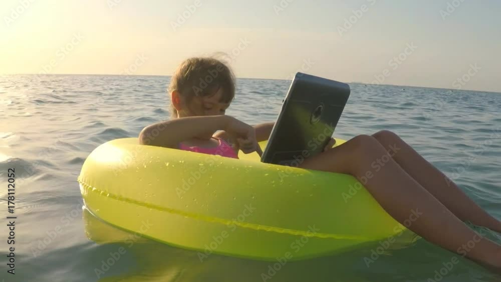 A child with a laptop on an inflatable circle is floating in the sea ...