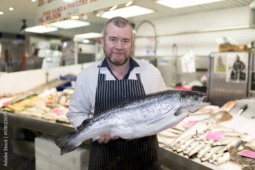 Foto de Male fishmonger wearing an apron holding large and whole salmon ...