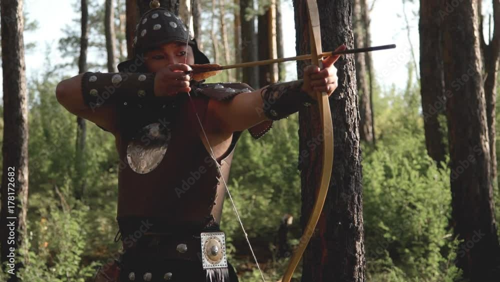 Archer with an eastern appearance aiming an arrow in forest. Mongolian ...