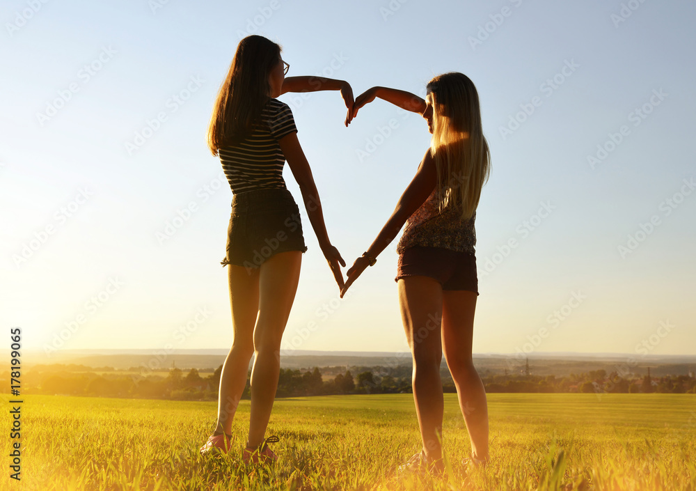 Young girls making heart symbol with their hands at sunset. Stock Photo ...