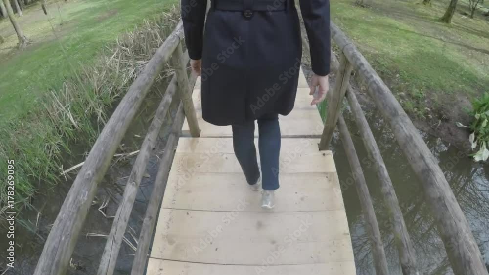 Woman model walk slowly over the small wooden bridge in the park. Slow ...