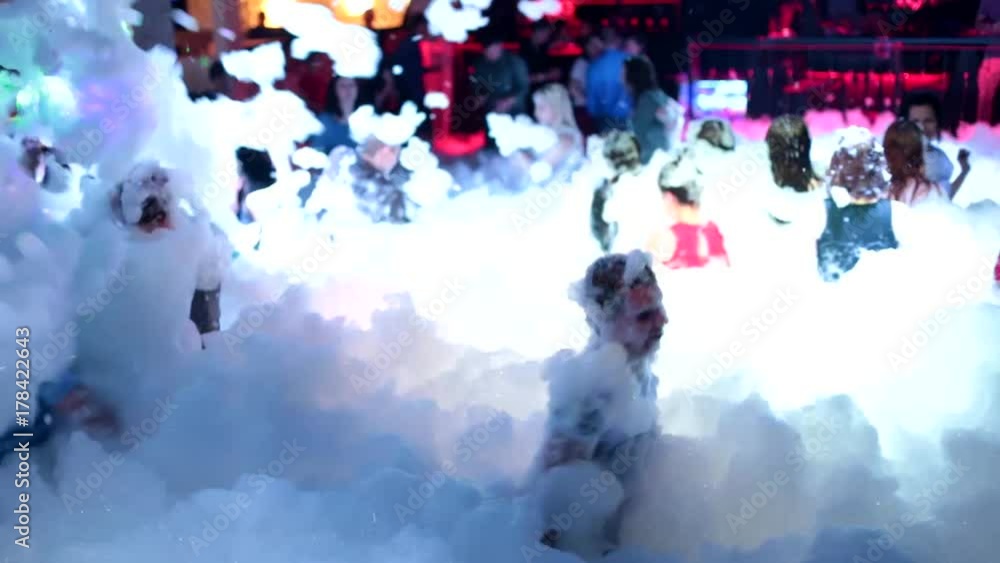 Foam party in a nightclub. A lot of foam on the dance floor. People ...
