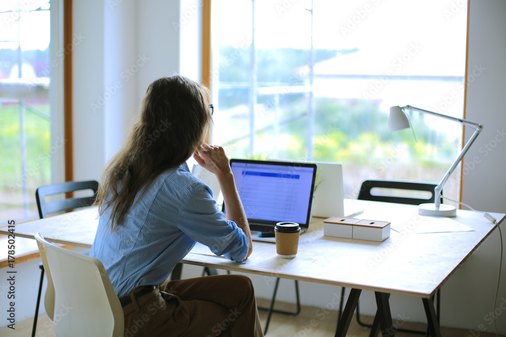 Young woman sitting in office table, looking at laptop computer screen ...