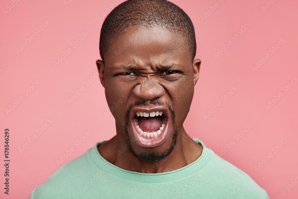 Furious African American male screams in despair, opens mouth widely ...