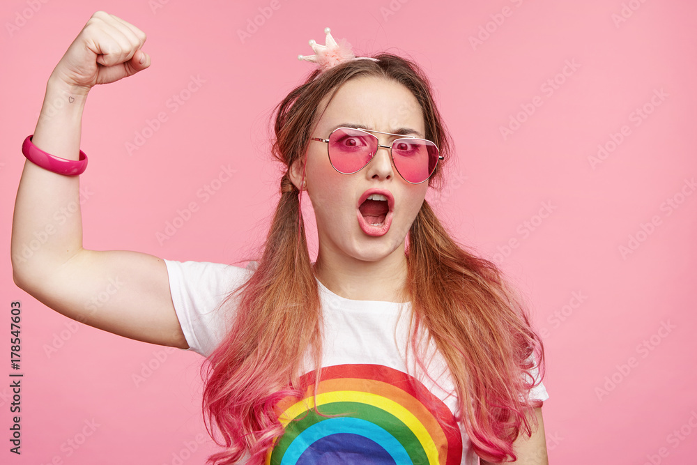 Arrogant pretty woman in pink eyewear, shows muscle on her hand, feels ...