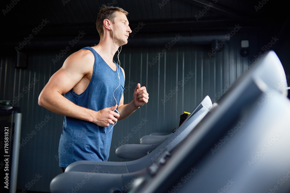 Side view portrait of muscular young man running on treadmill in modern ...