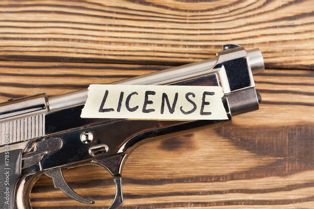 Inscription LICENSE on torn paper and glossy pistol on old rustic ...