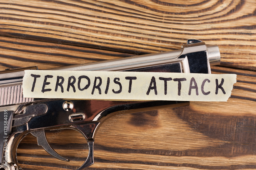 Inscription TERRORIST ATTACK on torn paper and glossy pistol on old ...