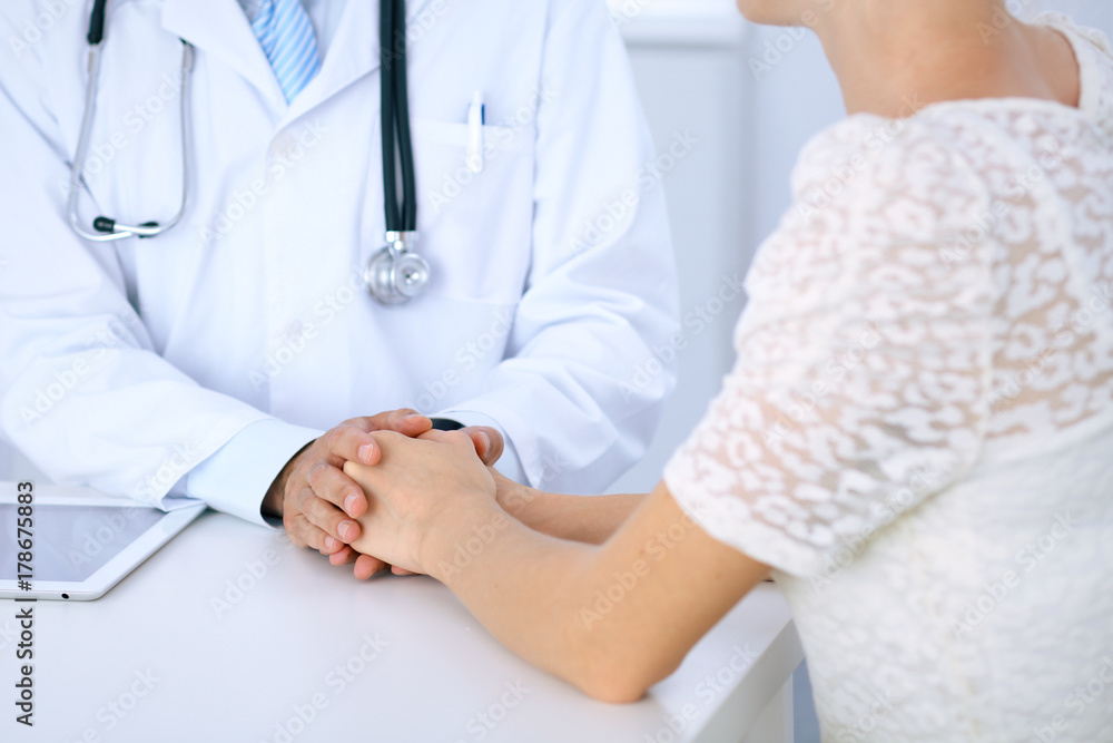 Doctor reassuring his female patient by touching her hands while ...