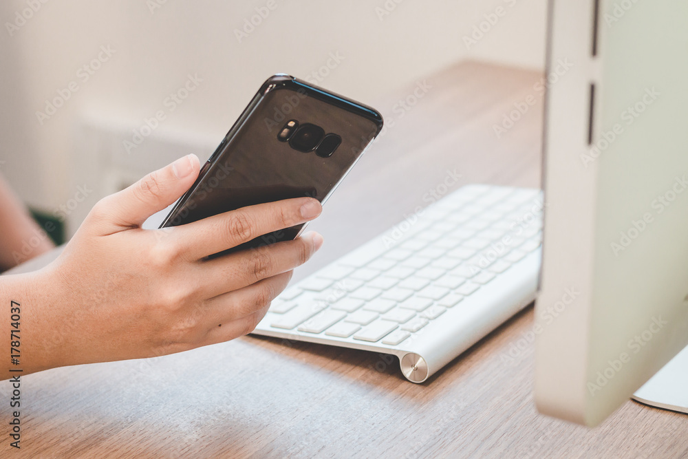 Hand holding black smart phone on back view in workspace Stock Photo ...
