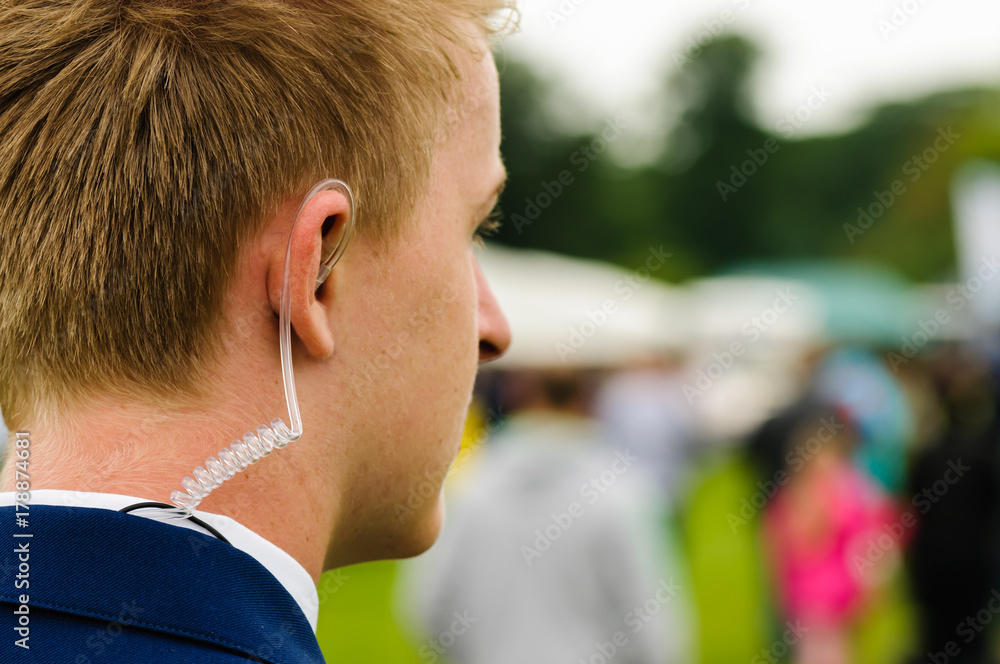 A young security guard wearing a coiled earpiece to listen to his two ...