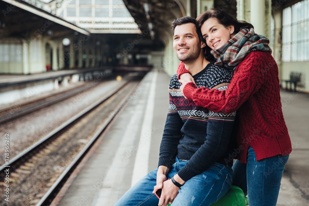 Pleasant looking female and male embrace each other stand near luggage ...