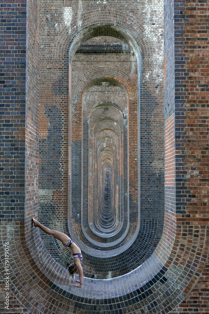 Female 20s performing a yoga back bend within the brick arches of a ...