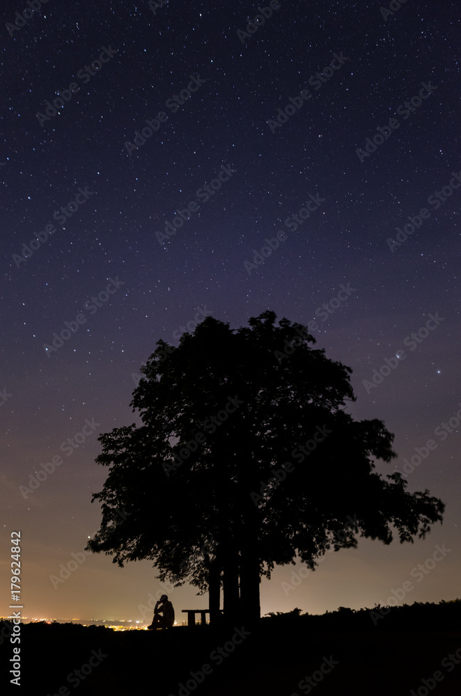 Silhouette of a man sitting and thinking under the tree at starry night ...