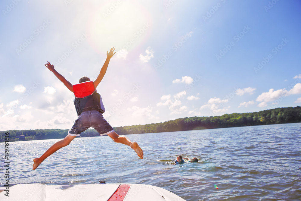 Kids jumping off a boat into the lake. Focus on boys legs and boat ...