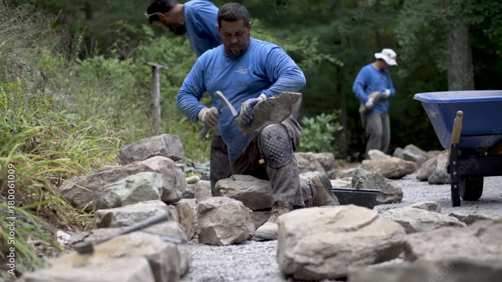 Chipping away at a large shale rock to make it fit a stone wall design ...