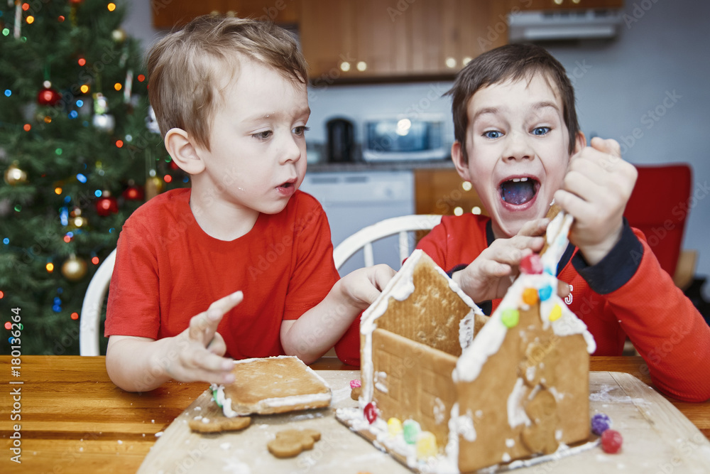 children eat gingerbread house and have fun. two cute boys enjoy ...