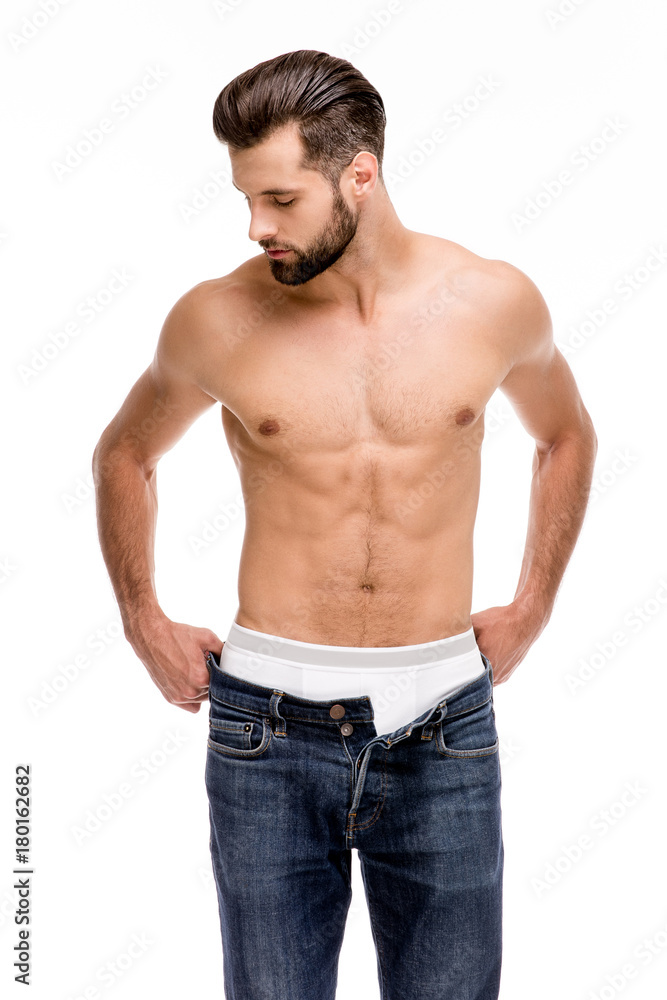 Perfect fit. Handsome shirtless young man taking off his jeans while ...
