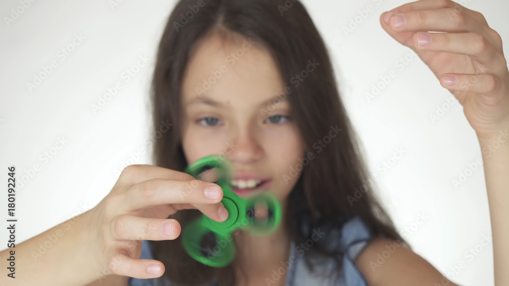 Beautiful cheerful teen girl playing with green fidget spinner on white ...