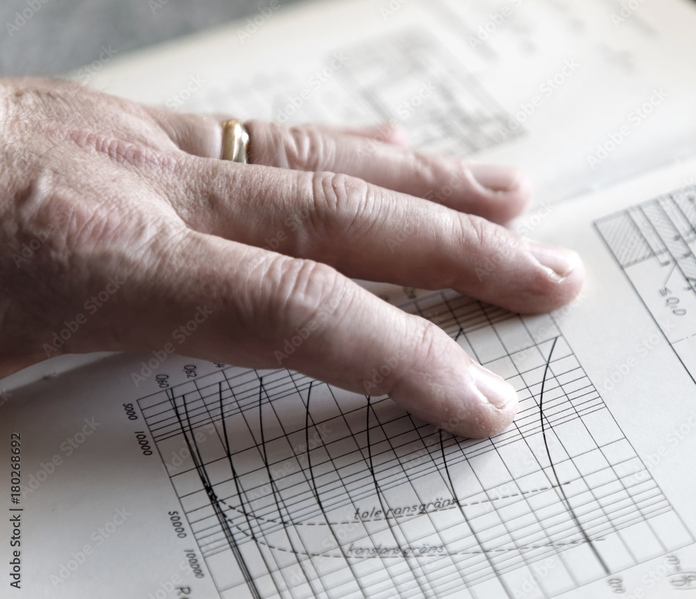 Hand of an engineer checking complicated formulas and charts in a ...