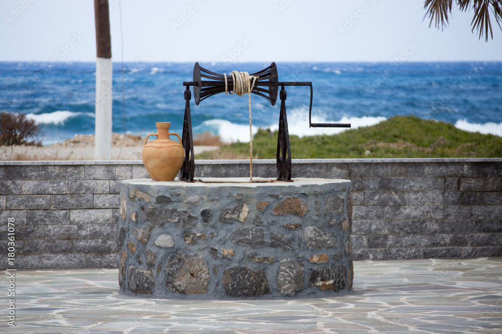 Ancient Greek water stone brick well and antic jug with sea background ...