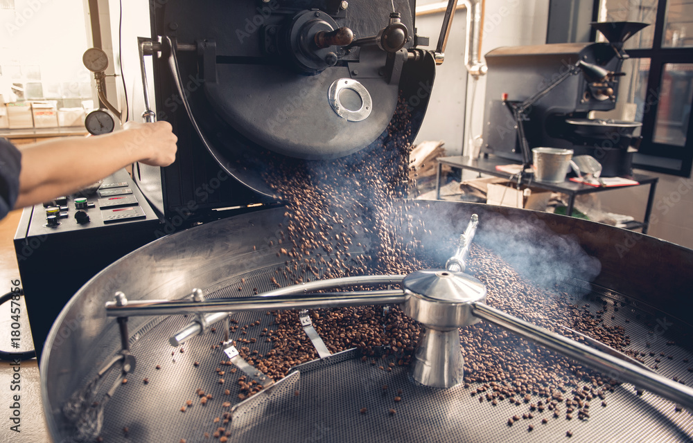 Male arm pressing button to open equipment. Coffee pouring from roaster ...