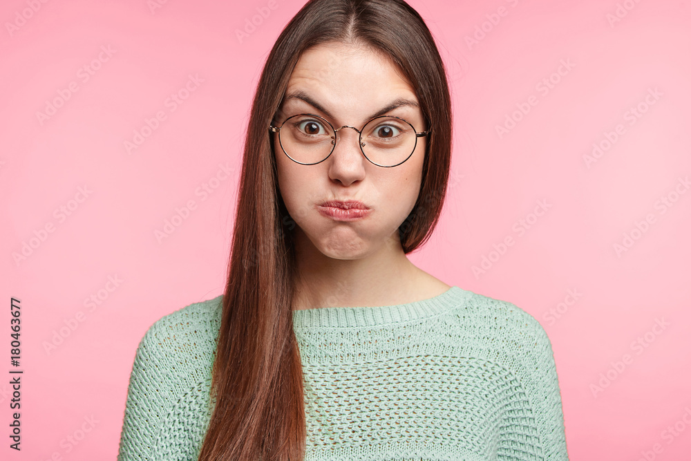 Annoyed Young Asian Female Blows Cheeks In Dissatisfaction Raises Eyebrows And Frowns Face