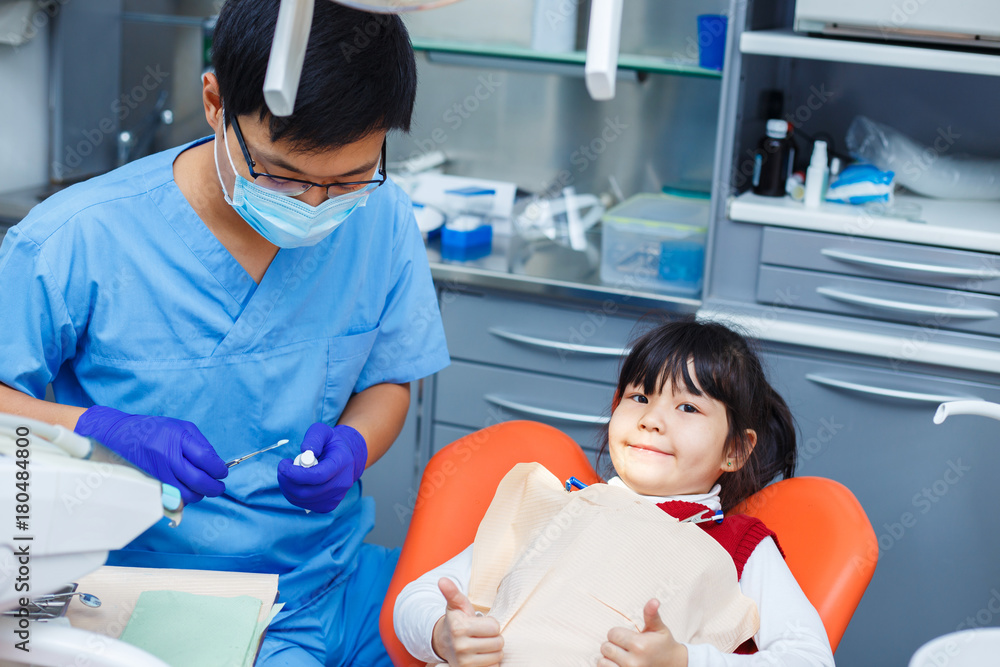 Little girl is sitting still in the dentist chair, smiling and showing ...