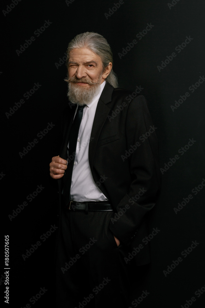 Old man in black suit and white shirt standing against black background ...