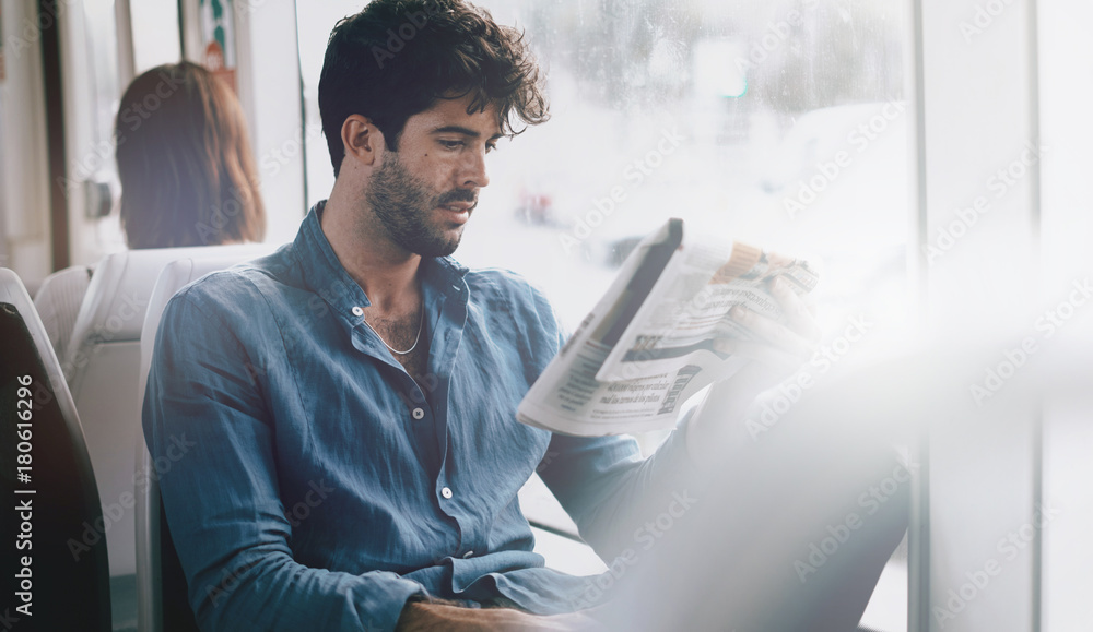 Young business man reading a newspaper while sitting in a city tramway ...